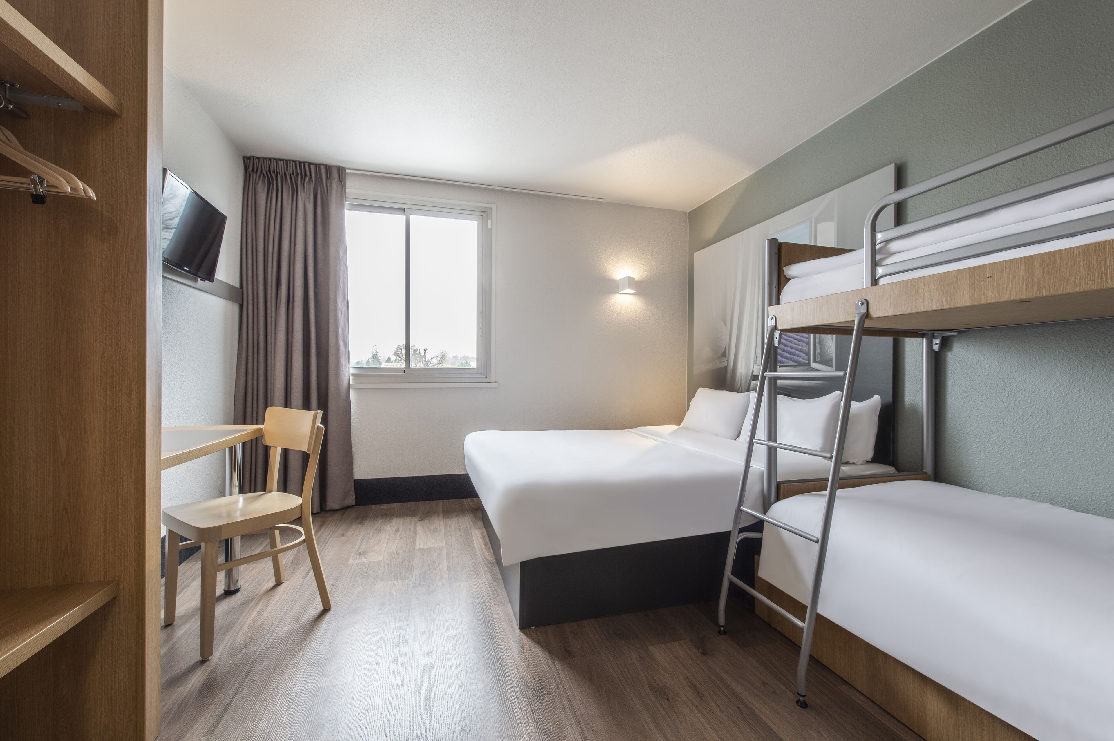 Quarto de hotel compacto com beliche, escrivaninha e cadeira.