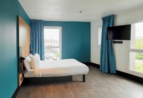 Quarto de hotel moderno com cama, televisão de tela plana, janela com cortinas e vista para a cidade.