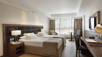 Quarto de hotel com duas camas, uma escrivaninha, uma cadeira, televisão e janela com cortinas.