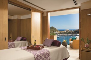 Quarto de hotel com duas camas, varanda com vista para o mar e barcos, e decoração em madeira.