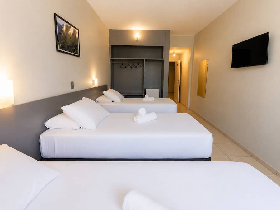 Quarto de hotel com duas camas, um guarda-roupa, uma televisão e um quadro na parede.