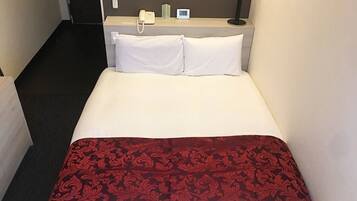 Quarto de hotel com cama, telefone ao lado da cama, relógio digital e abajur na mesa de cabeceira.