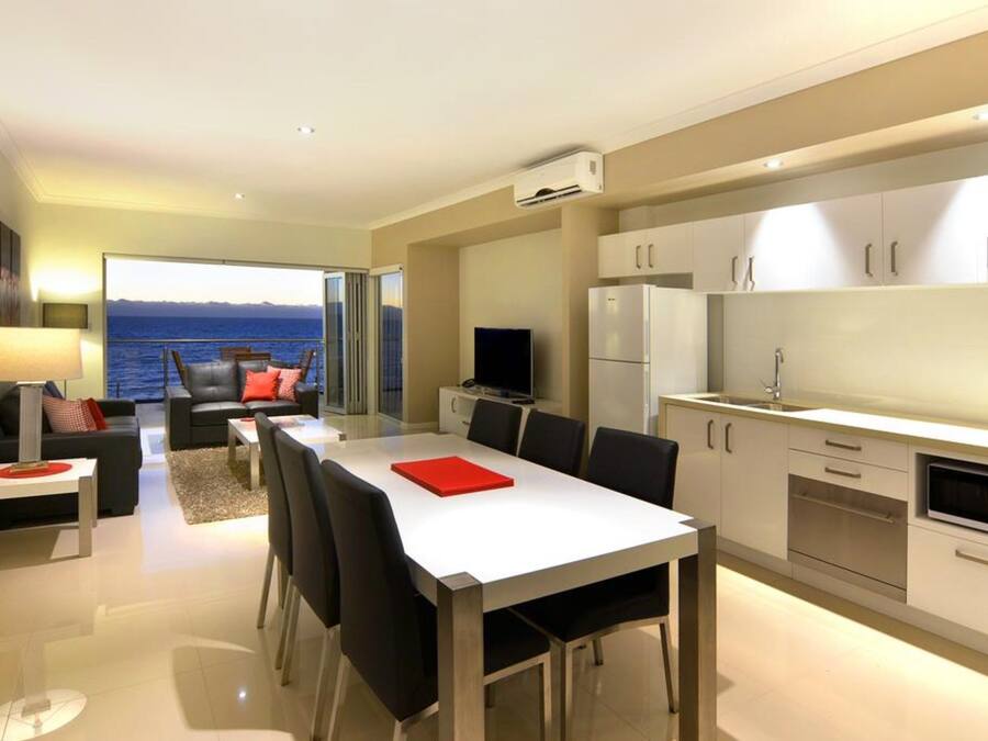 Cozinha moderna com área de refeições, TV e vista para o mar.