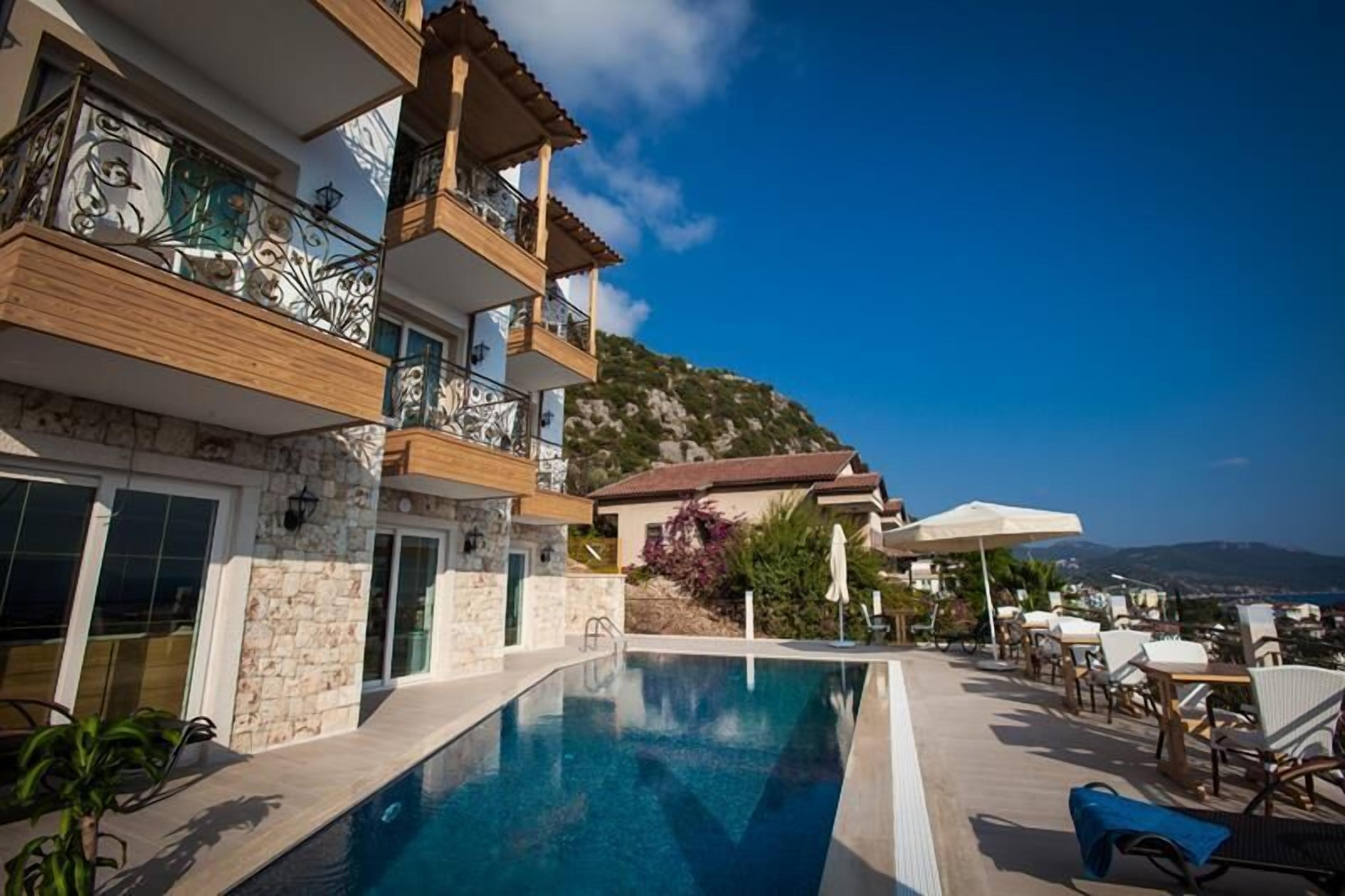 Área junto à piscina com vista clara para o mar e montanhas, varandas de madeira e mobiliário para áreas externas.