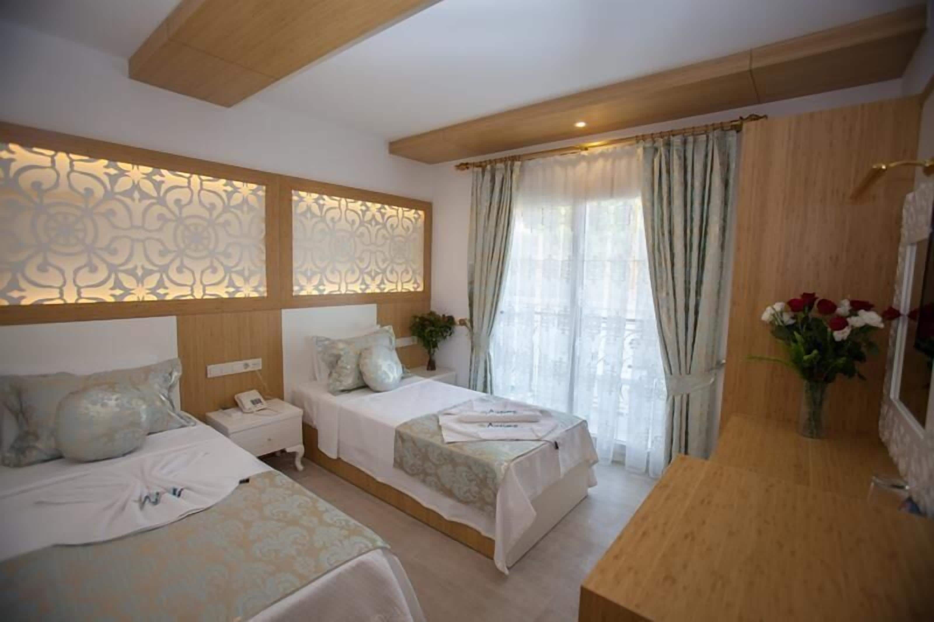 Quarto de hotel com duas camas, teto de madeira, mesa de cabeceira com telefone e um vaso com flores.