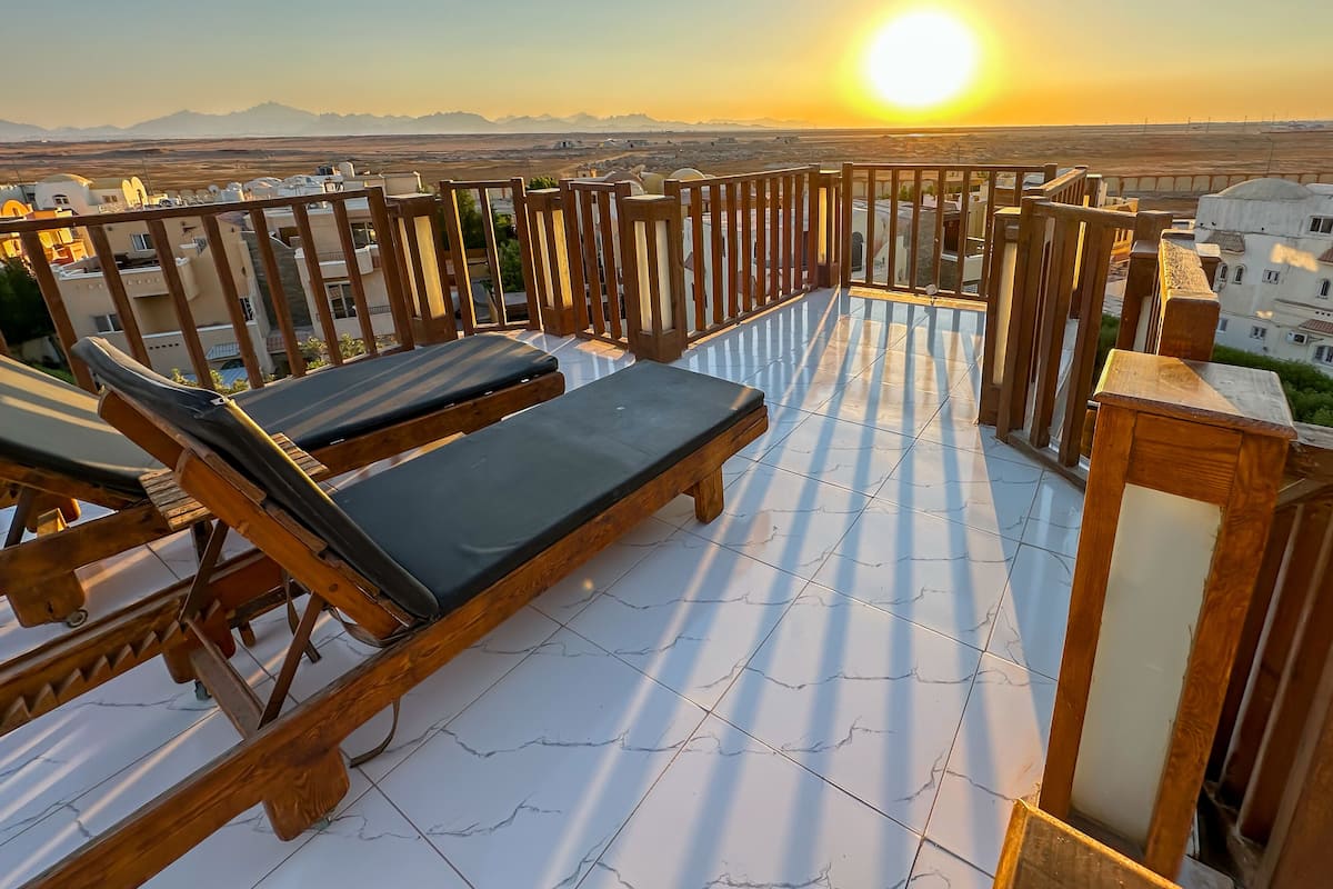 Terraço com guarda-corpos de madeira, duas poltronas de descanso e vista para montanhas ao longe durante o pôr do sol.