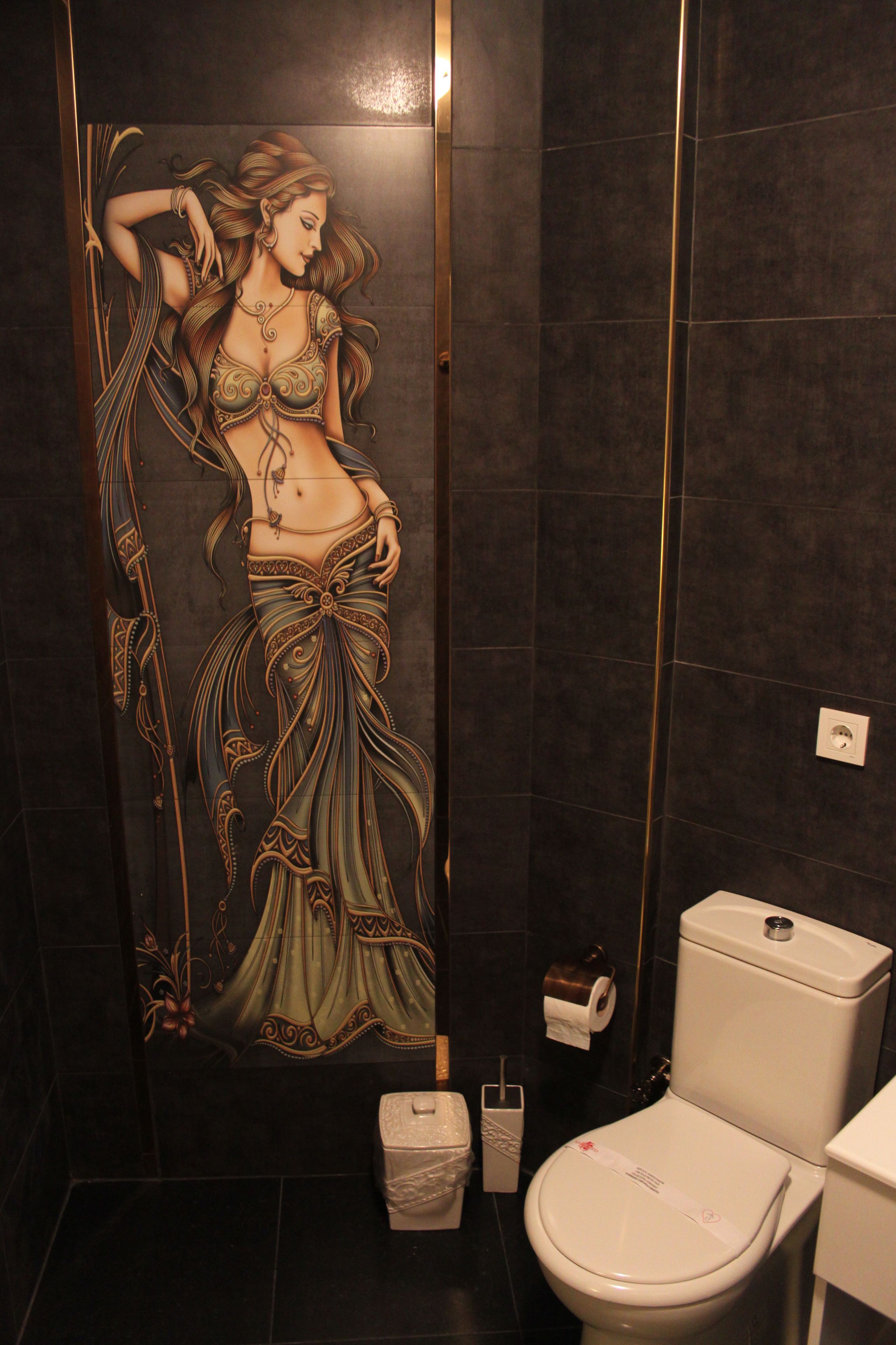 Casa de banho com um mural decorativo, uma sanita e um contentor de lixo.