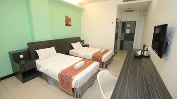 Quarto de hotel com duas camas, uma escrivaninha, uma cadeira, uma televisão e uma kitchenette.