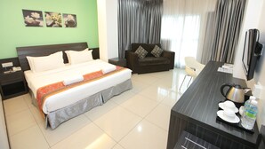 Quarto de hotel com cama, sofá, escrivaninha com chaleira e chávenas, e televisão.