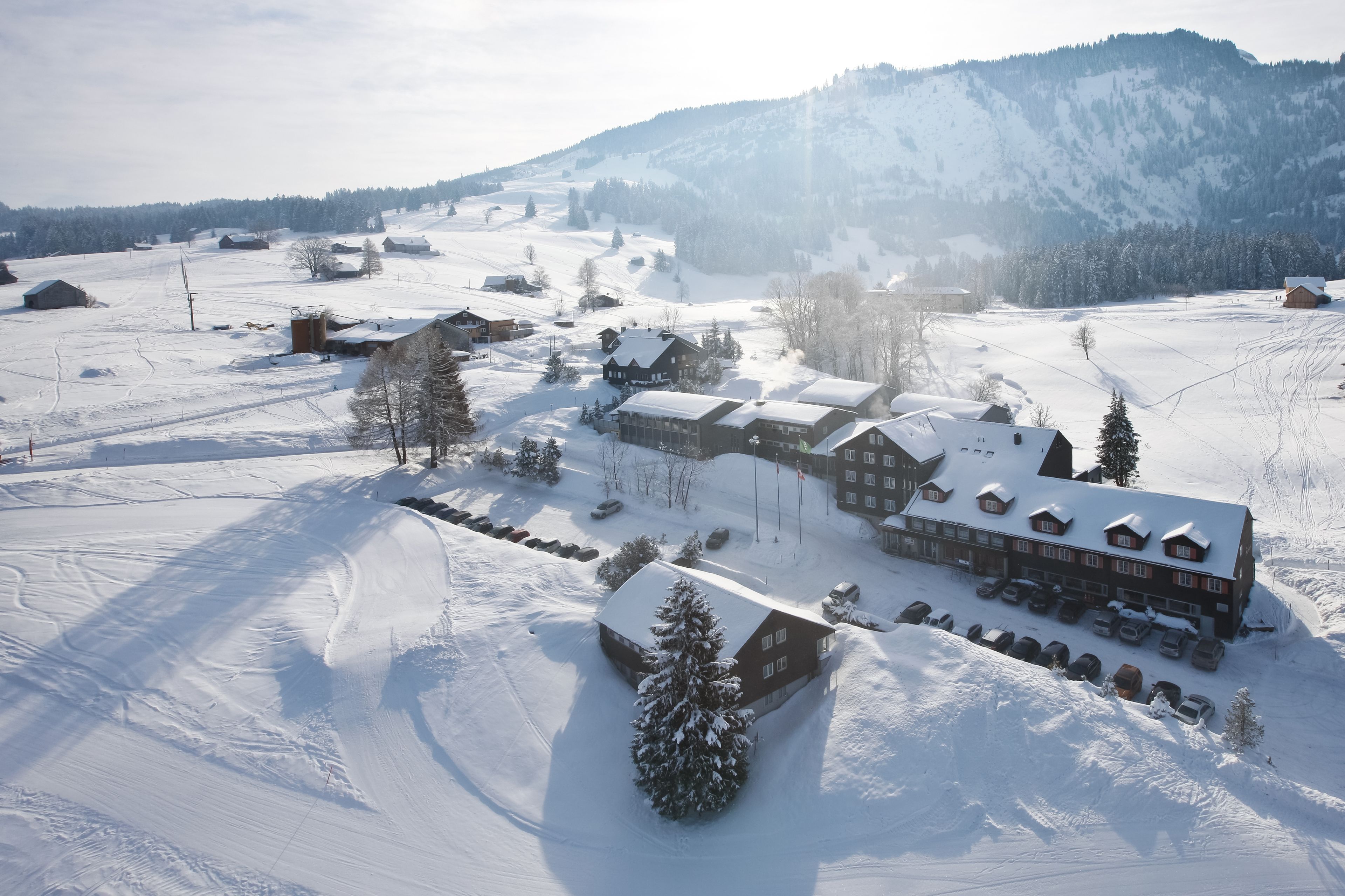 Uma pousada coberta de neve com vários edifícios, área de estacionamento e montanhas ao fundo.
