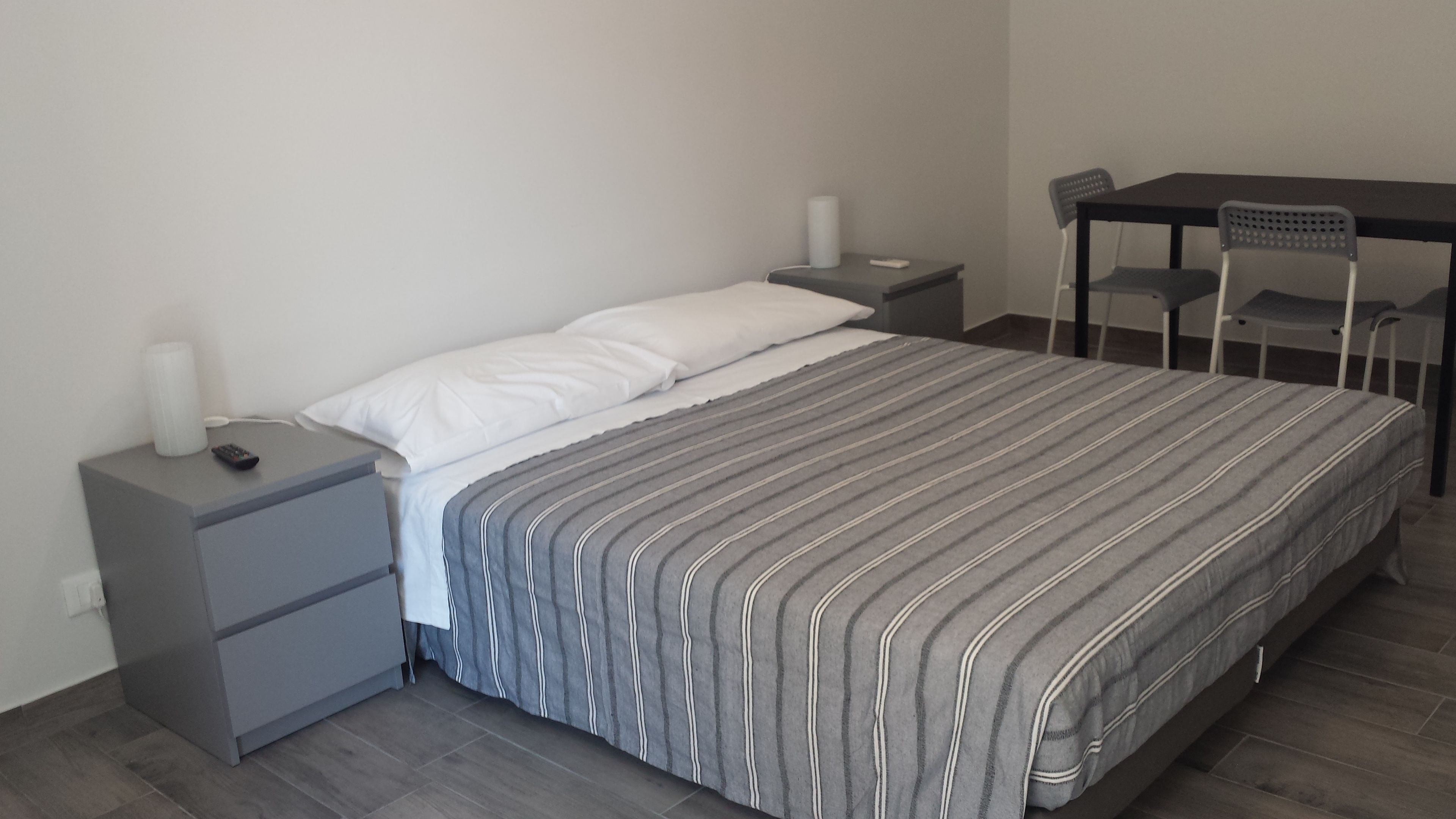 Um quarto com uma cama, uma mesa de cabeceira, uma escrivaninha e uma cadeira.