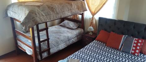 Quarto com uma cama beliche, uma cama de solteiro e uma mesinha de cabeceira com abajur.