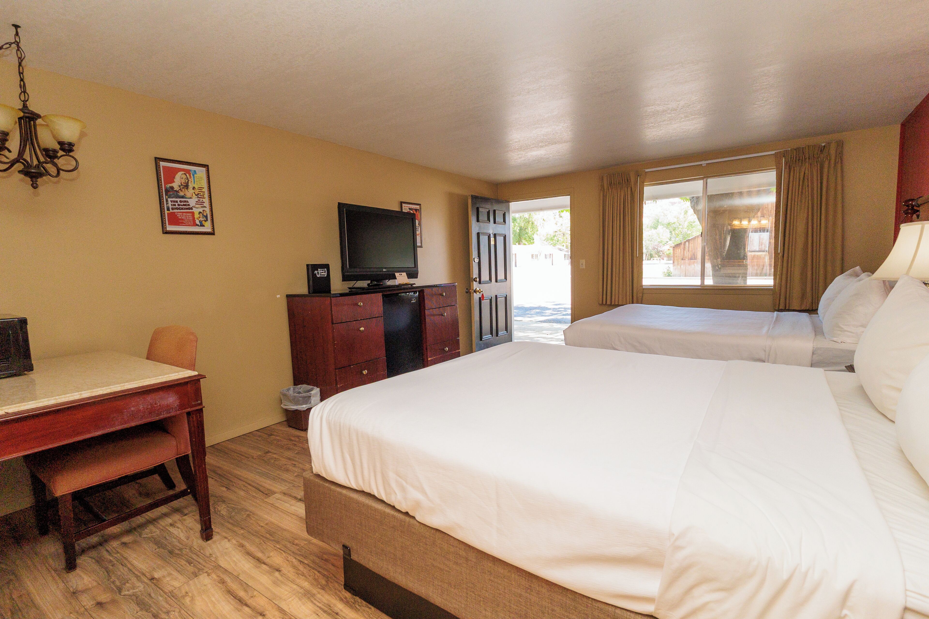 Quarto de hotel com cama, escrivaninha, televisão e janela com cortinas.