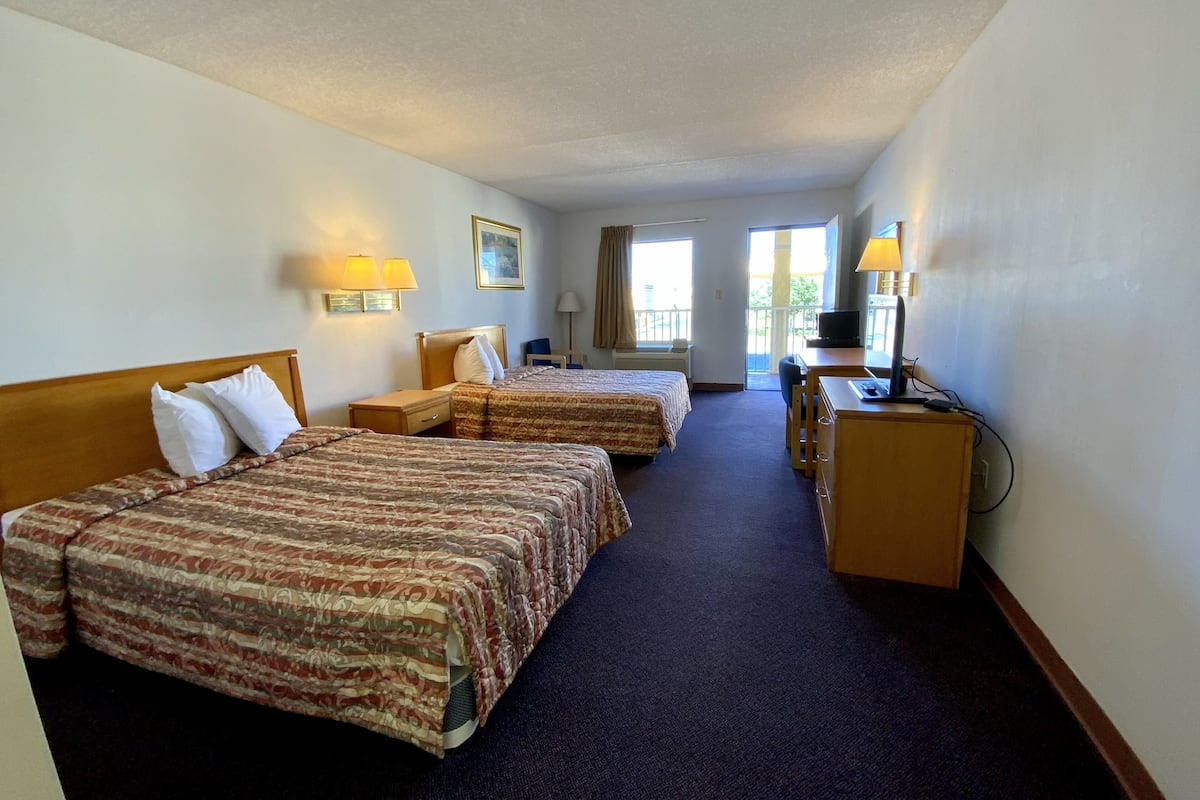 Quarto de hotel com duas camas, uma escrivaninha, uma cadeira e uma televisão.