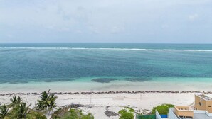Vista da praia com águas turquesa cristalinas, areal dourado e vegetação ao primeiro plano.