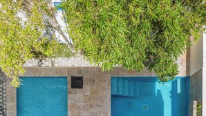 Uma área moderna de piscina ao ar livre com duas piscinas separadas, paredes de pedra e um espaço de estar com vista para a paisagem urbana.
