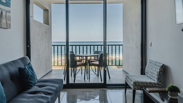 Uma sala de estar moderna com uma porta de vidro deslizante que dá para uma varanda com vista para a praia.