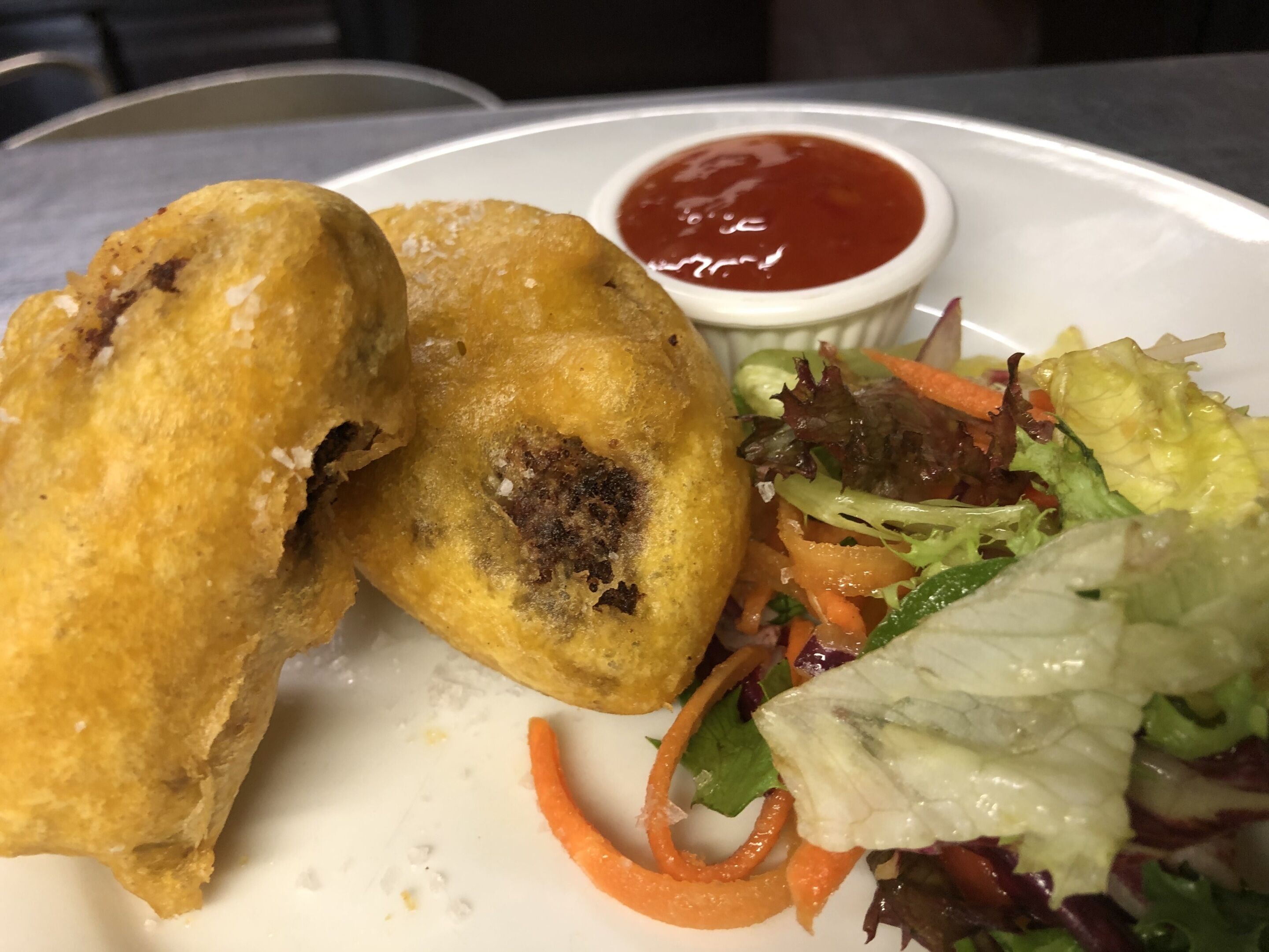 Um prato com comida frita, uma salada e uma pequena tigela de molho.