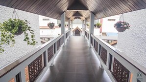 Um corredor coberto com chão de azulejos, paredes brancas e vasos suspensos.