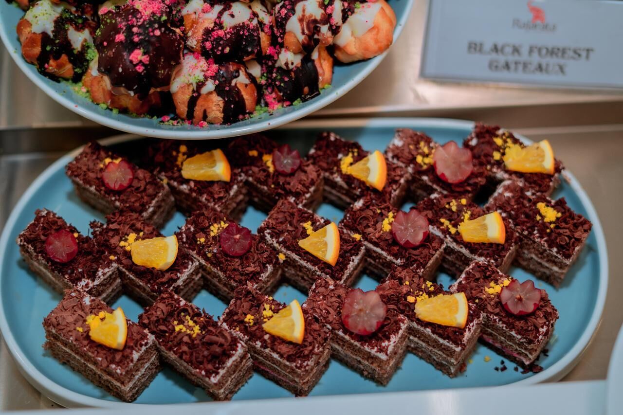 Exposiç ão de sobremesas com doces de chocolate e um letreiro que diz 'BLACK FOREST GATEAUX'.