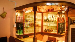 Uma área de bar com prateleiras cheias de garrafas de bebidas e copos, um balcão de madeira e uma placa indicando o bar.