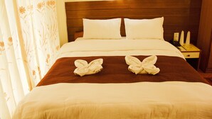 Quarto de hotel com cabeceira de madeira, roupa de cama branca e duas toalhas sobre a cama.
