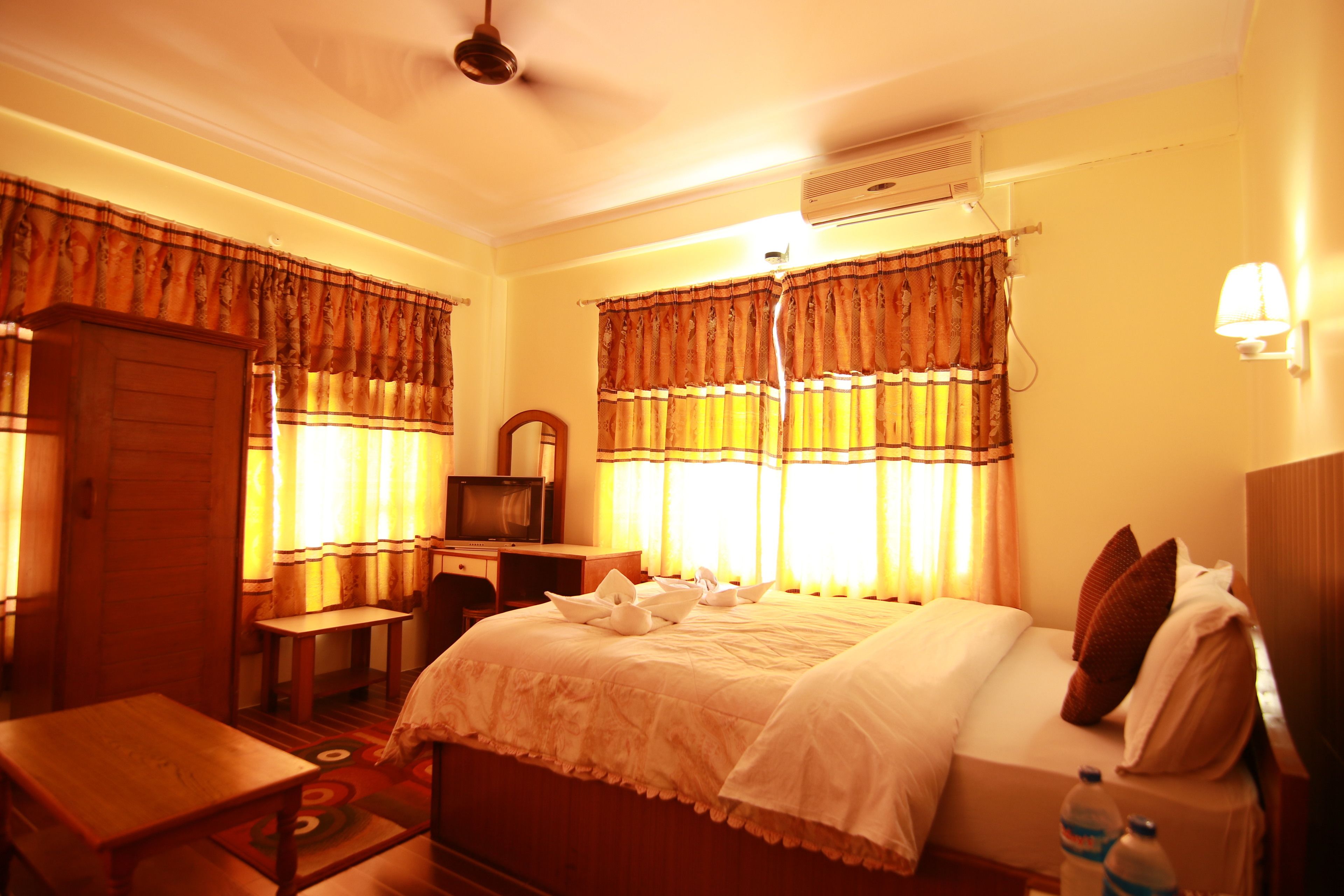 Quarto de hotel com cama, escrivaninha, cadeira e televisão.