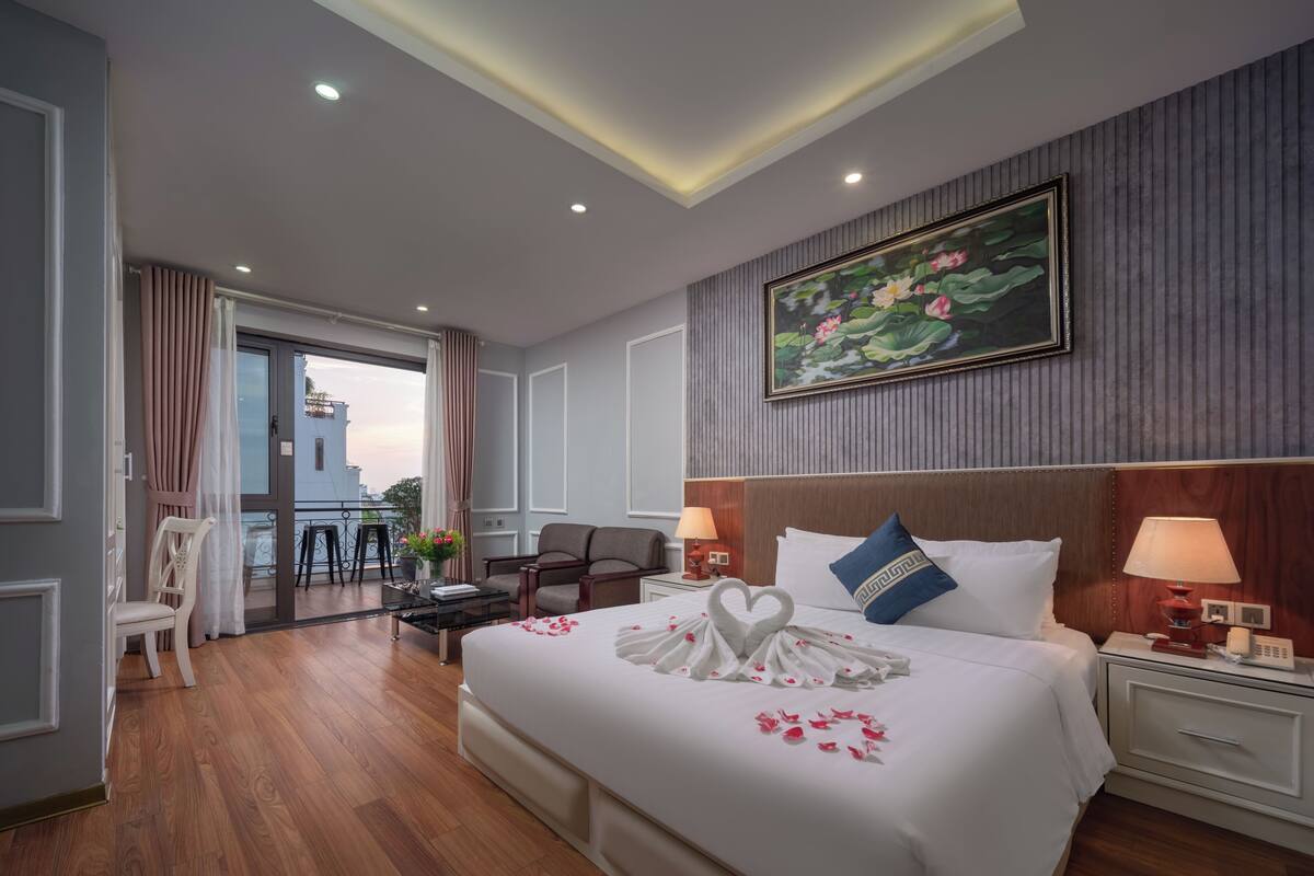 Quarto de hotel com uma cama grande, um quadro de flores, uma escrivaninha e uma cadeira.