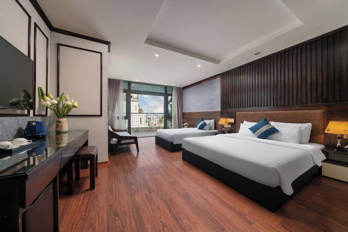 Quarto de hotel com duas camas, uma escrivaninha, uma cadeira, uma cafeteira e um vaso com flores.