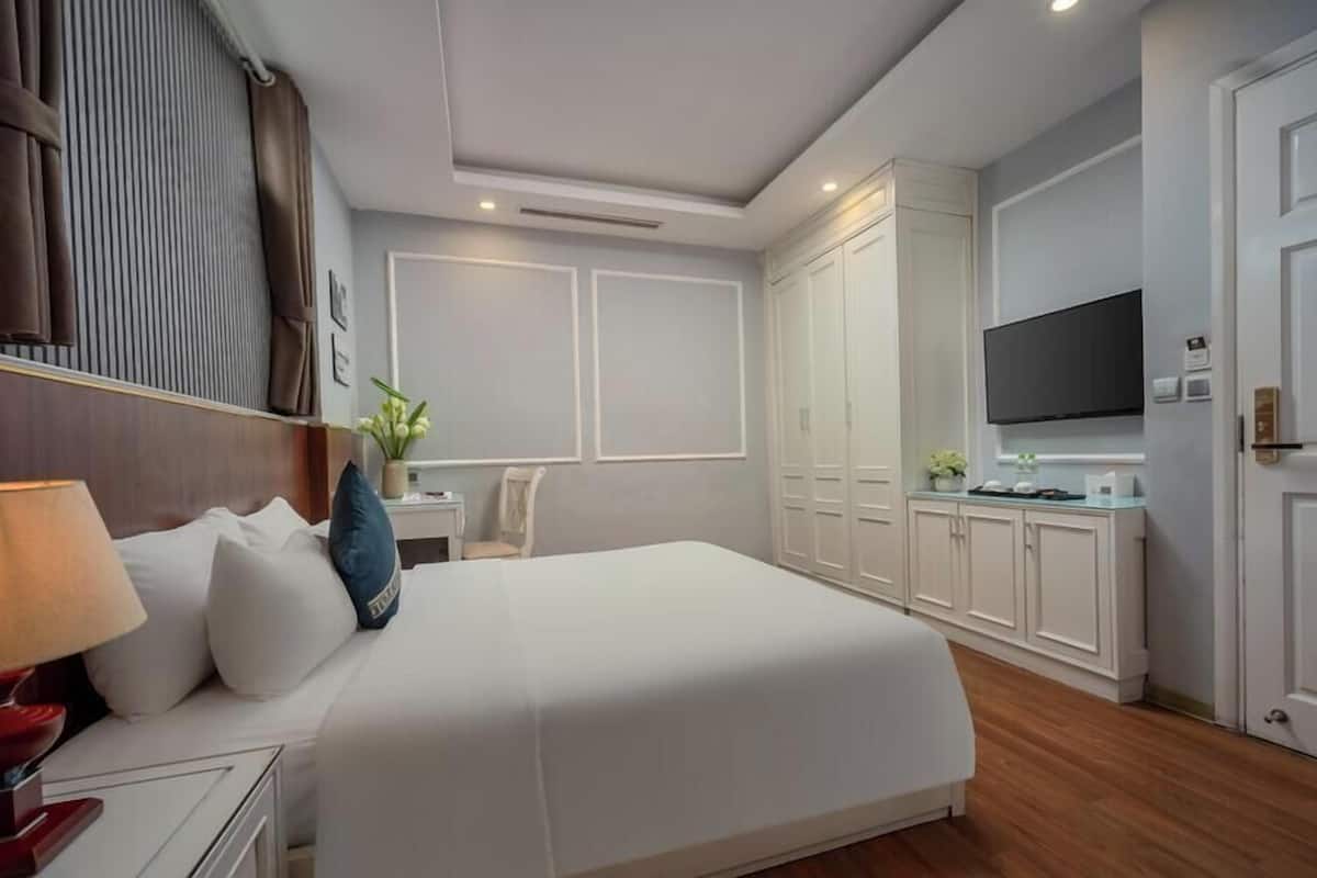 Quarto de hotel com cama, televisão, escrivaninha e guarda-roupa.