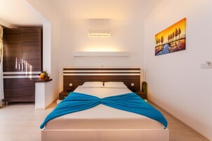Quarto de hotel moderno com uma cama grande, uma mesinha de cabeceira, ar condicionado fixado na parede e um quadro.