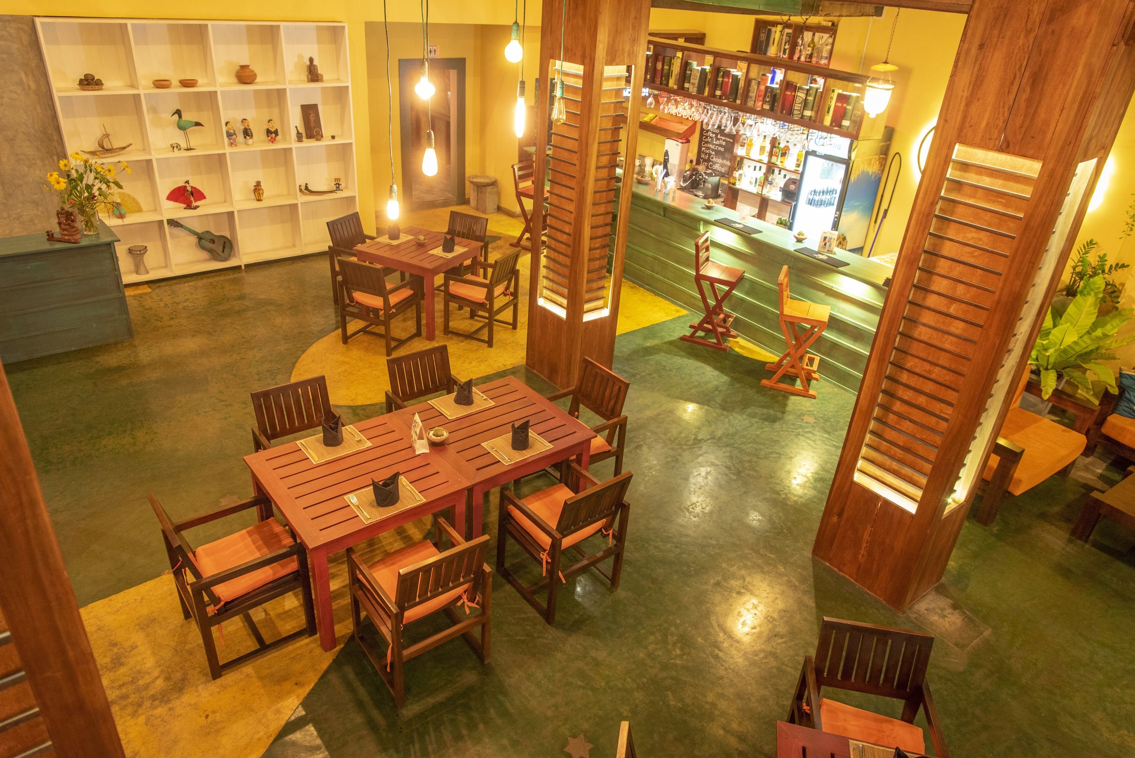 Restaurante com mesas e cadeiras de madeira, um espaço de bar e prateleiras com objetos decorativos.