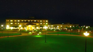 Um hotel com um edifício central, várias janelas e uma entrada bem iluminada.