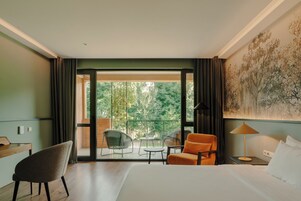 Quarto de hotel com cama, escrivaninha, cadeira, mesa e varanda com cadeiras.