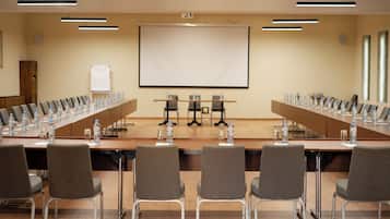 Uma sala de conferências com uma mesa comprida, várias cadeiras, garrafas de água, uma tela de projetor e um quadro branco.