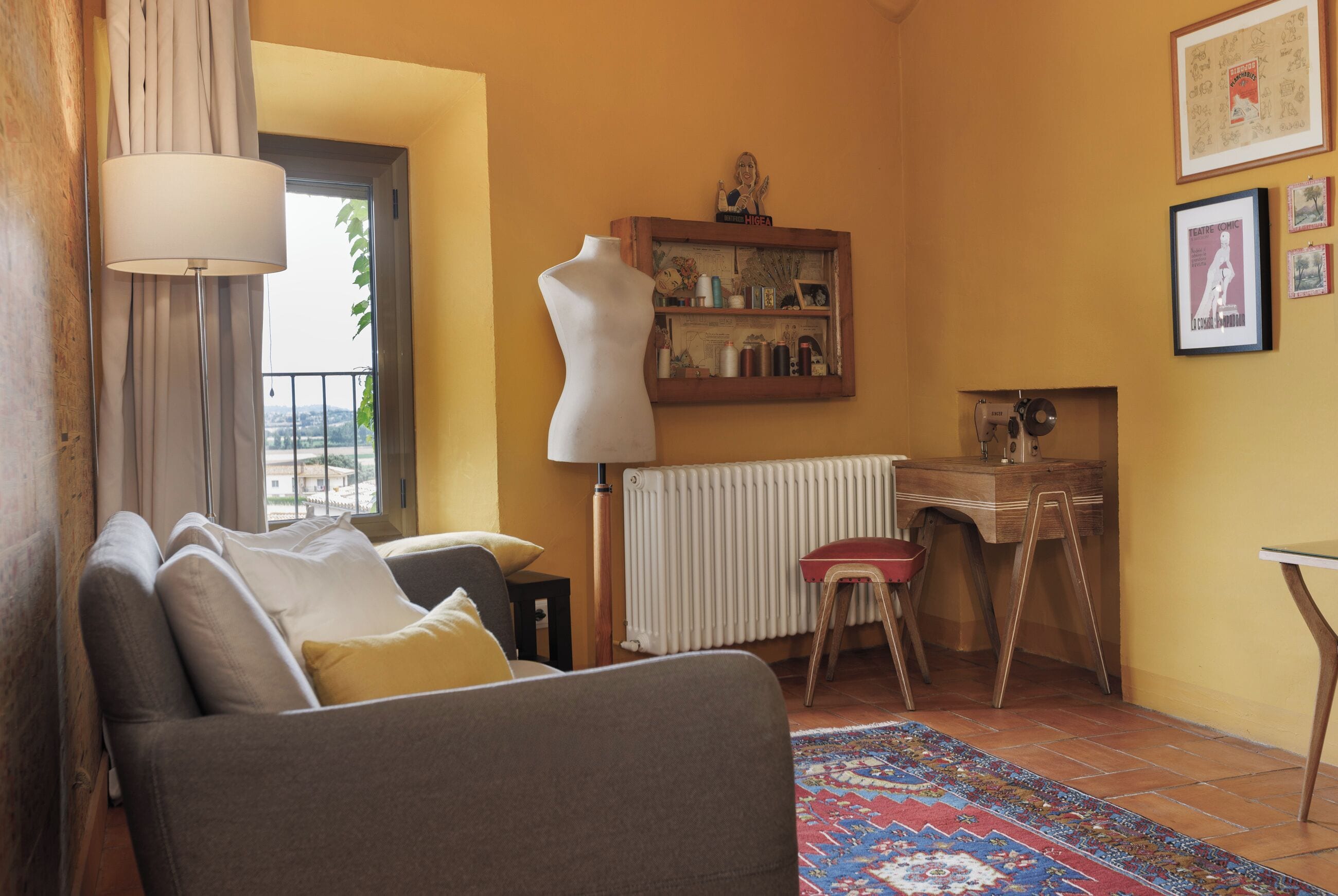 Uma sala de estar com sofá, luminária, radiador, escrivaninha e uma estante com diversos objetos.