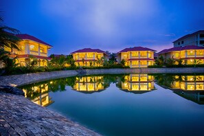 Resort com vários edifícios, piscina refletora e vegetação exuberante.