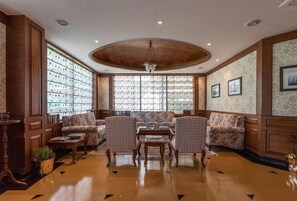 Um hall com teto de madeira, área de estar central com mesa e cadeiras, e uma parede com quadros emoldurados.