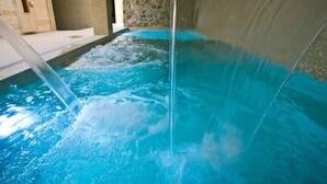 Uma banheira de hidromassagem com jatos, paredes de pedra e portas de madeira.