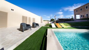 Piscina com deck de pedra, área gramada com espreguiçadeiras e um edifício com fachada em pedra.