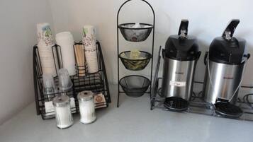 Uma cozinha com pratos de papel empilhados, uma cafeteira, saleiro e pimenteiro, e uma cesta de metal.