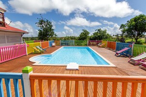 Um deck de madeira com piscina, cercas coloridas e espreguiçadeiras.