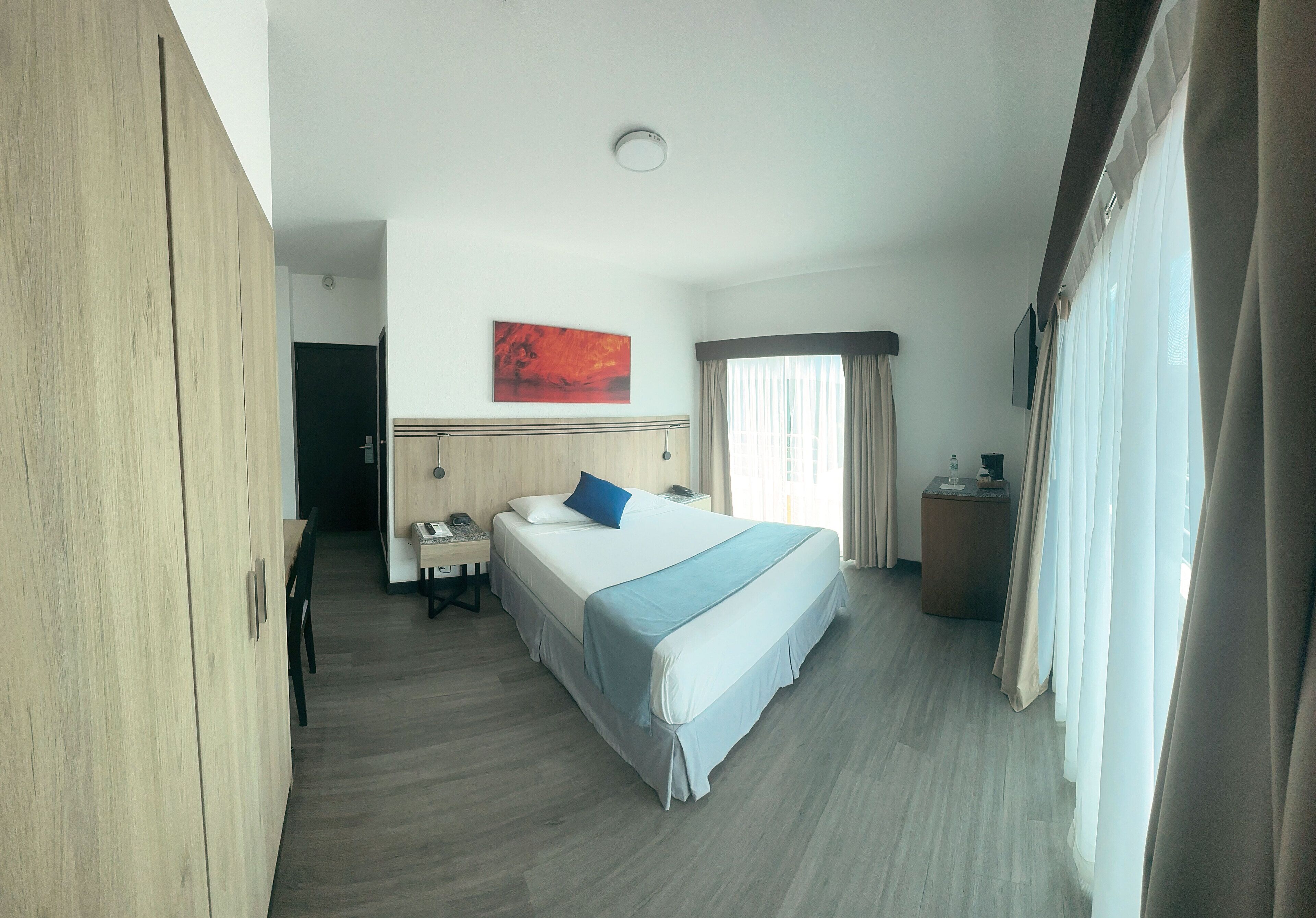 Quarto de hotel com cama, mesa de cabeceira e escrivaninha com cadeira.
