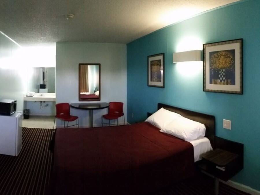 Quarto de hotel com cama, escrivaninha com cadeira, televisão, espelho e duas fotografias emolduradas na parede.