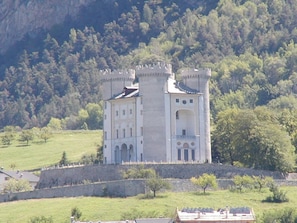 Uma construção que lembra um castelo, com uma torre central, cercada por uma muralha de pedra e situada numa encosta arborizada.