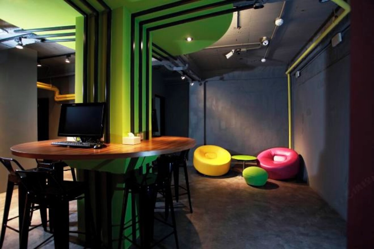 Quarto moderno com uma mesa de madeira redonda, um computador e poltronas confortáveis coloridas.