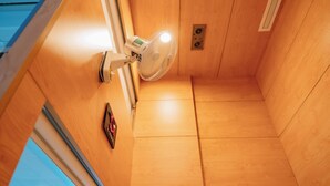Quarto de madeira com um ventilador, um interruptor de luz e uma ventilação na parede.