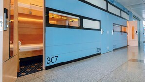Corredor moderno de hotel com parede azul, quarto 307 numerado e área de estar com bancos de madeira.