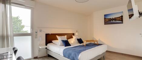 Quarto de hotel moderno com cama, mesa de cabeceira e escrivaninha com cadeira.