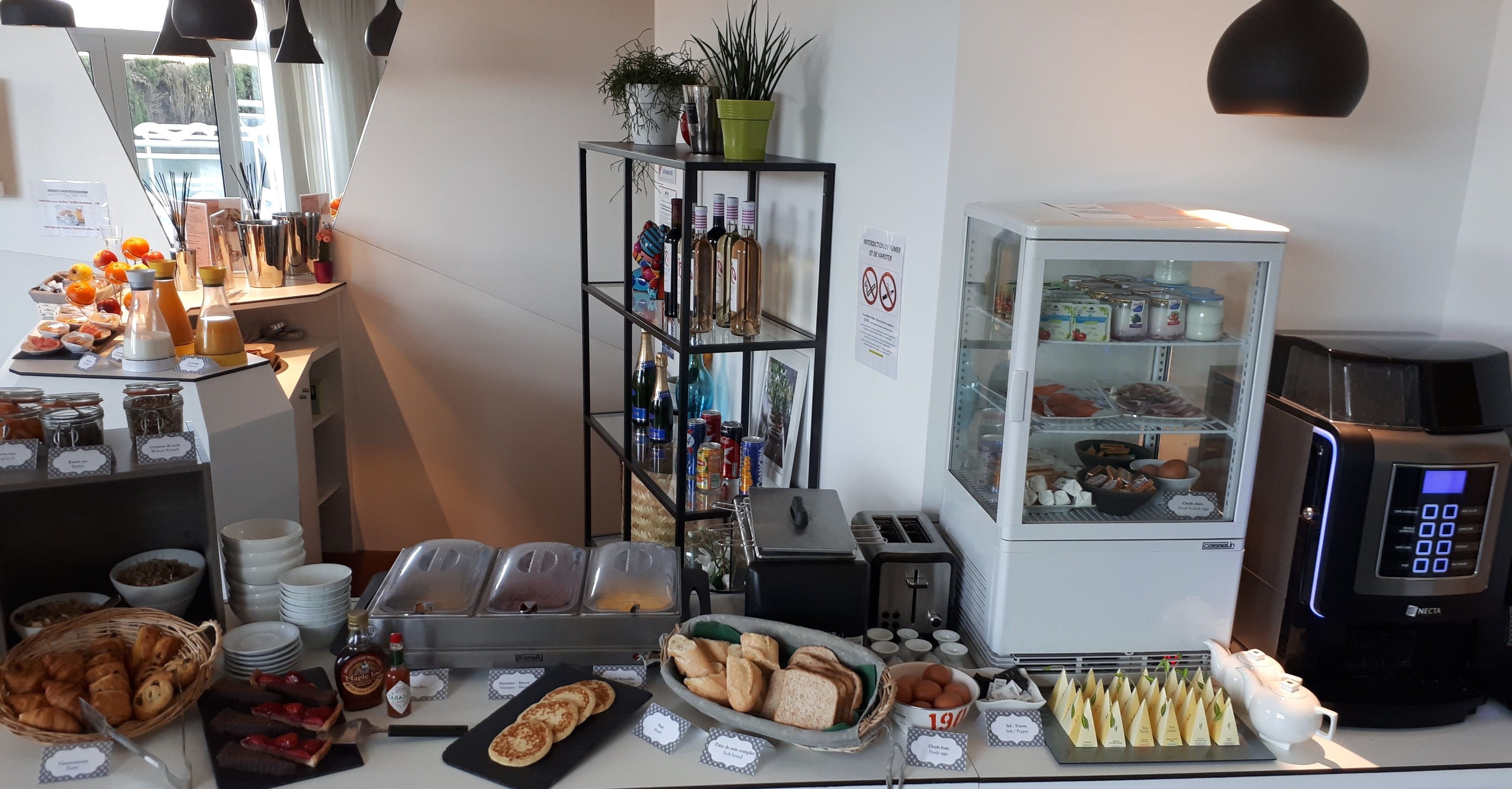 Um buffet de café da manhã com diversos alimentos, uma geladeira e uma máquina de café.